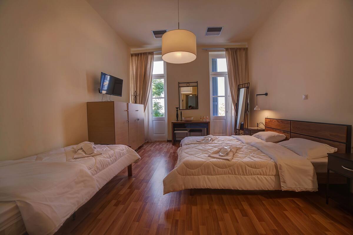 Quarto de hotel com duas camas, televisão, escrivaninha e espelho.