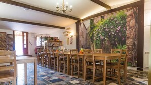 Uma área de refeições com mesas e cadeiras de madeira, piso de azulejos estampados e um grande mural na parede retratando um jardim.