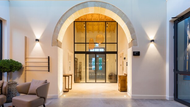 Um hall de hotel moderno com entrada em arco, balcão de recepção e área de estar com planta em vaso.
