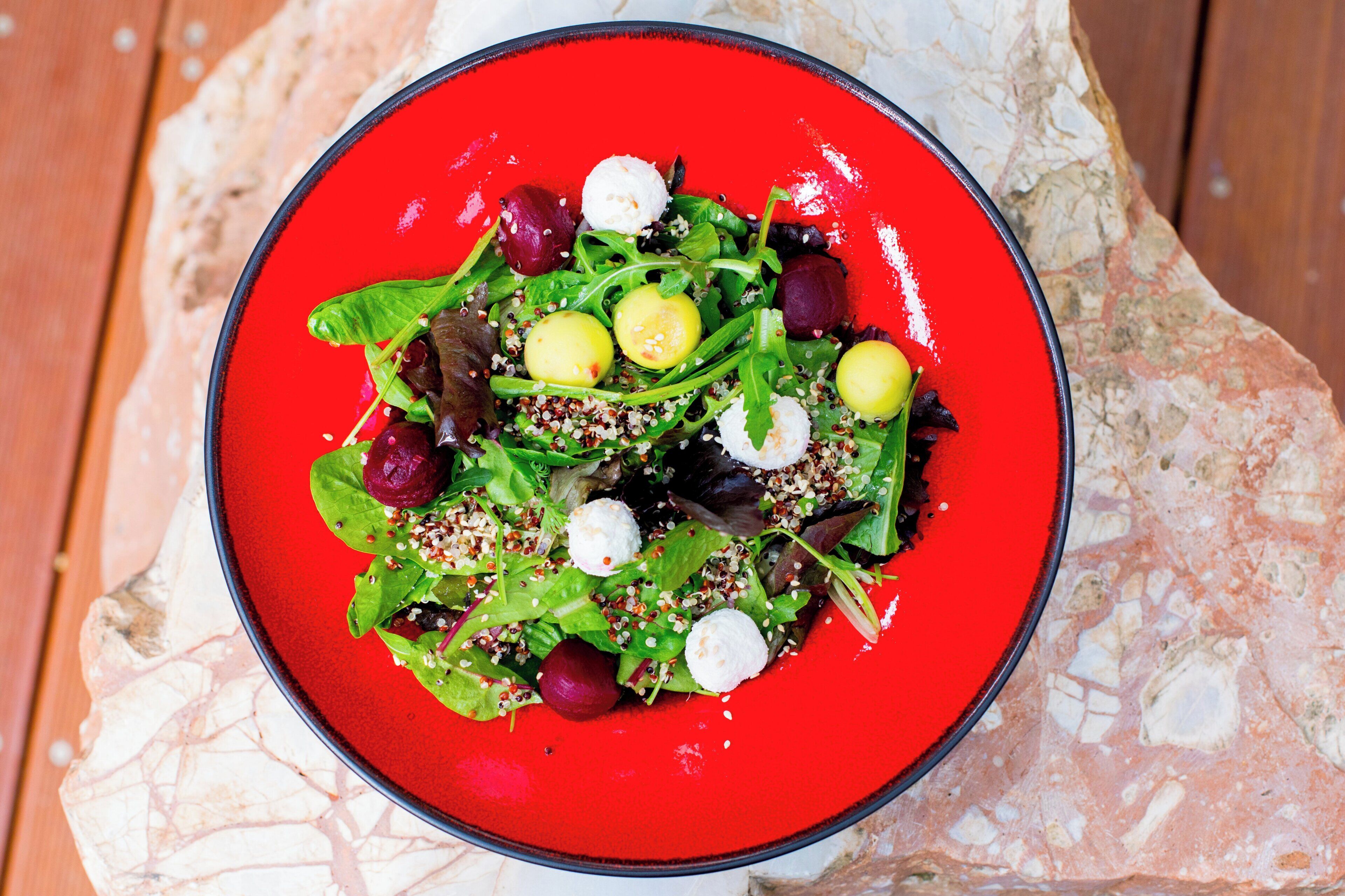 Uma tigela vermelha com salada sobre uma superfície de pedra.