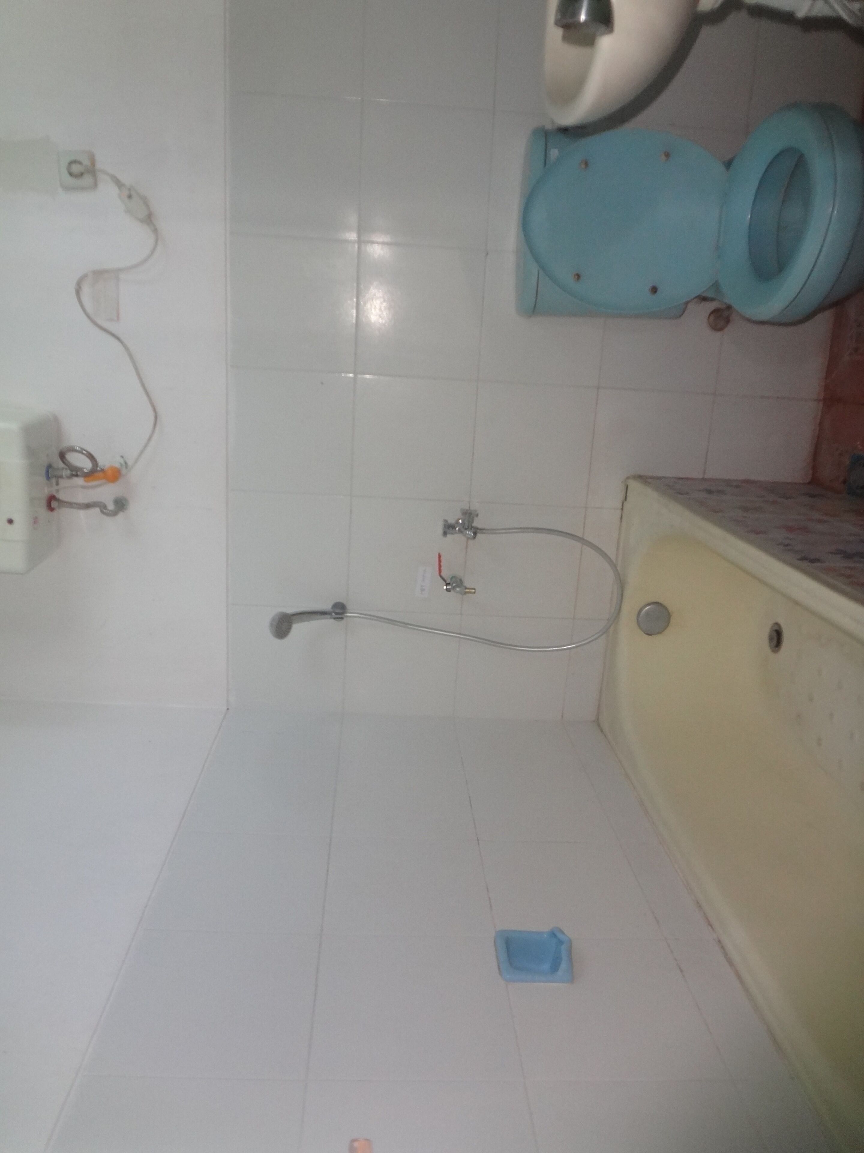 Casa de banho com chão em azulejos brancos, sanita azul e área de duche com chuveiro.