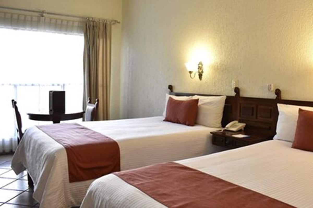 Quarto de hotel com duas camas, uma mesinha de cabeceira com telefone e uma cadeira.