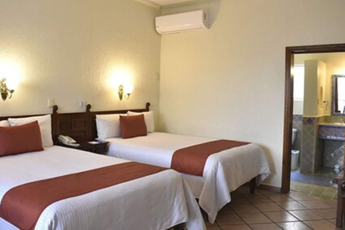 Quarto de hotel com duas camas, cabeceira de madeira, telefone e banheiro visível através de uma porta.