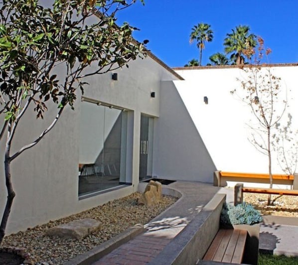Uma casa moderna com um pátio, um banco e uma árvore.
