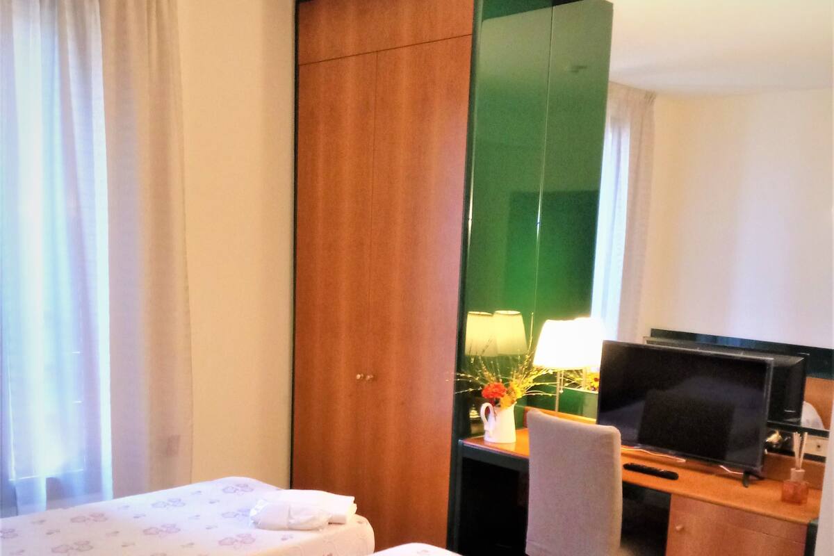 Quarto de hotel com duas camas, uma mesa com computador, televisão e espelho.