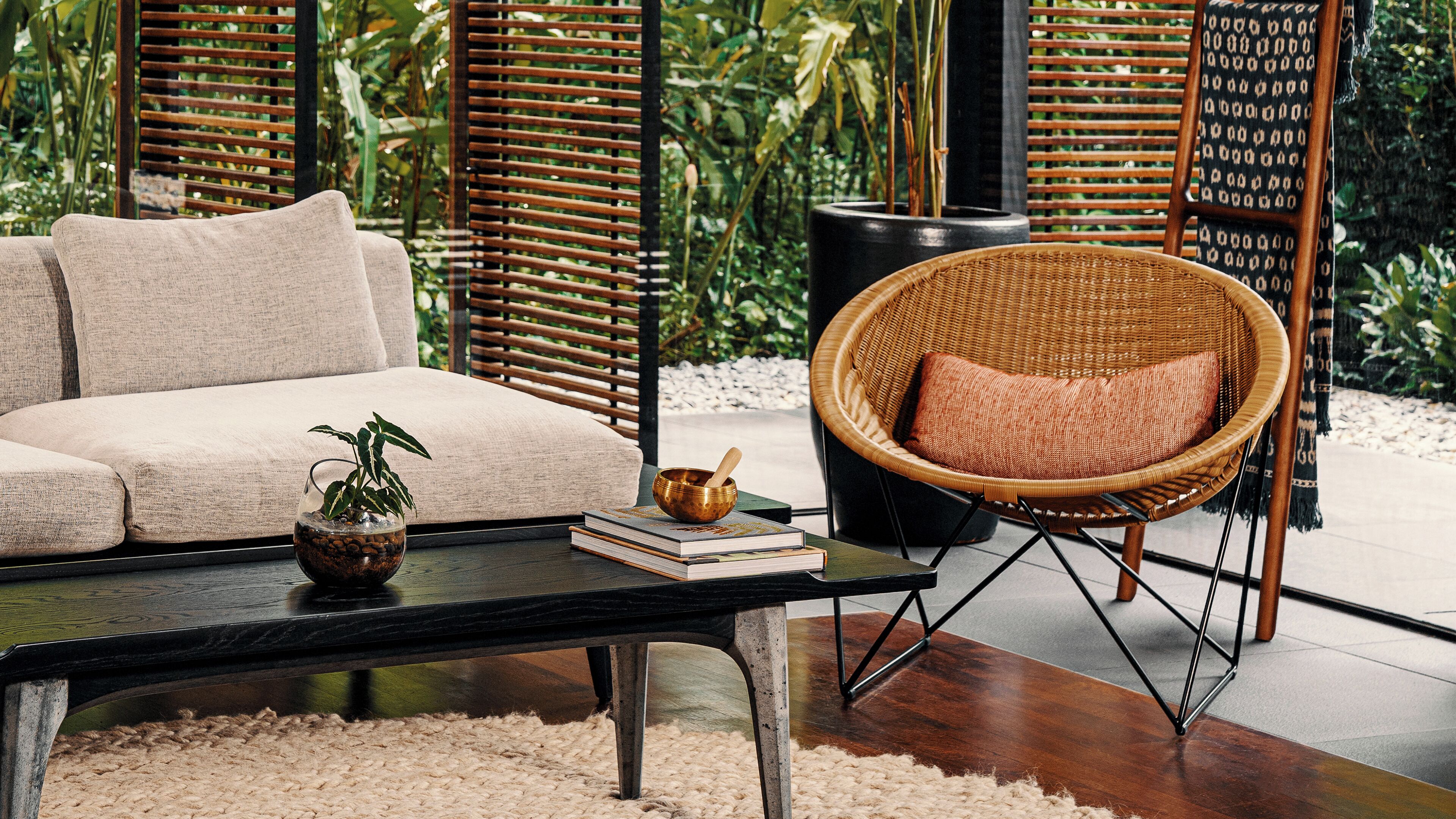 Uma sala de estar moderna com um sofá, uma poltrona de vime, uma mesa de centro e um vaso com planta.
