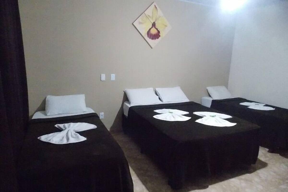 Quarto de hotel com três camas, cada uma com lençóis e toalhas brancas.