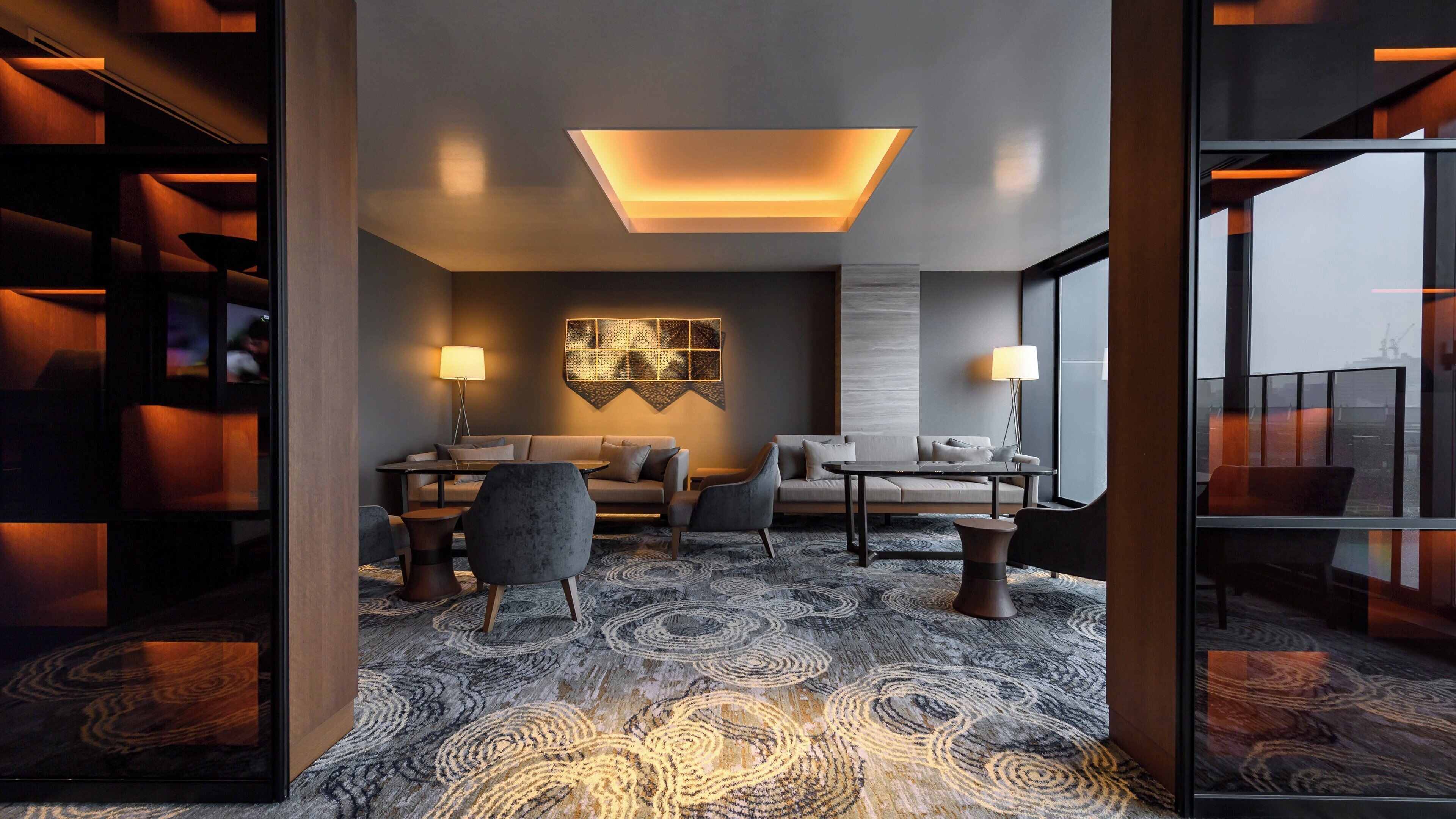 Quarto de hotel moderno com sofá, poltronas, mesa de centro e tapete estampado.