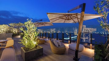 Terraço no telhado com área de estar externa, guarda-sóis e vista para o horizonte da cidade e para a água.