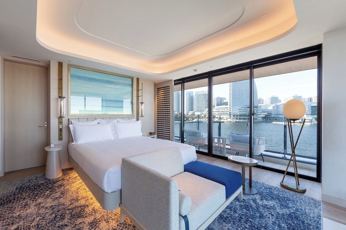 Quarto de hotel moderno com uma cama grande, área de estar, vista da cidade e uma janela ampla.
