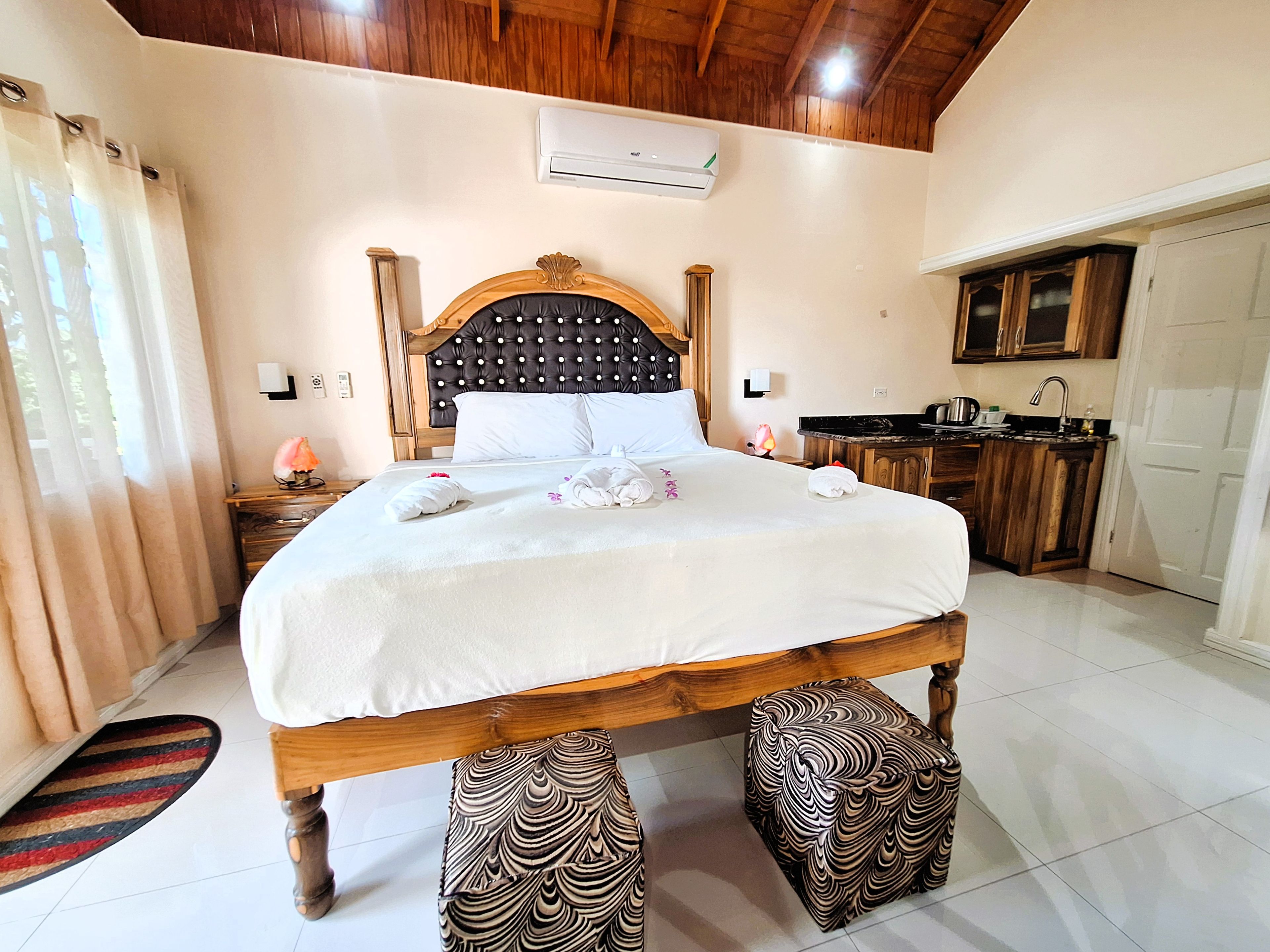 Quarto de hotel com cama de madeira, pequeno espaço com cozinha e banheiro.