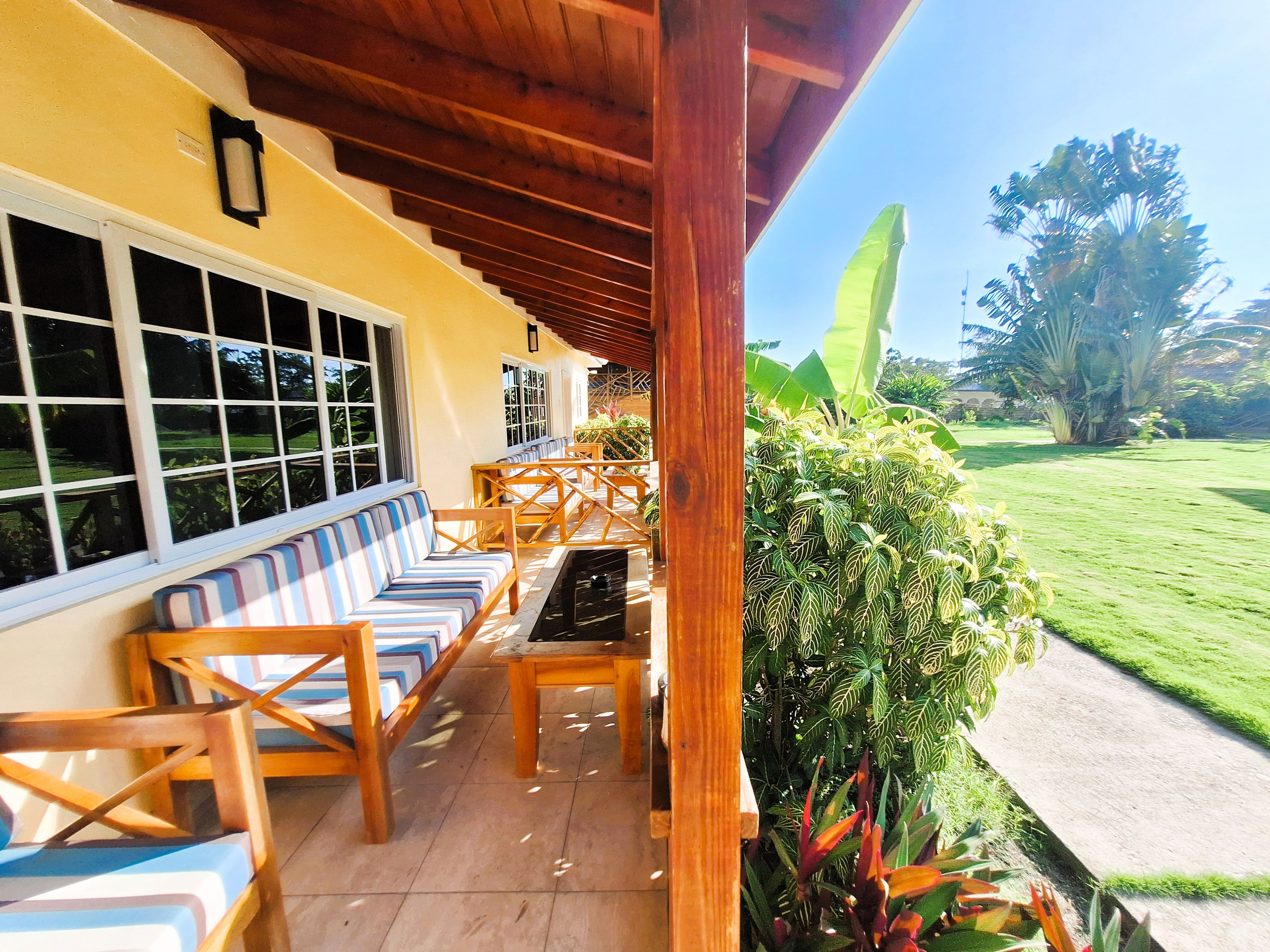 Uma área de estar ao ar livre com móveis de madeira e vista para um jardim bem cuidado.