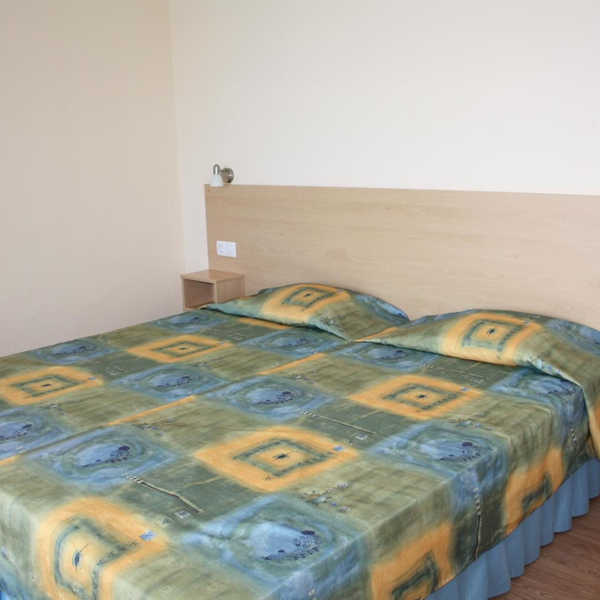 Uma cama de solteiro com cabeceira, mesa de cabeceira e tomada na parede.