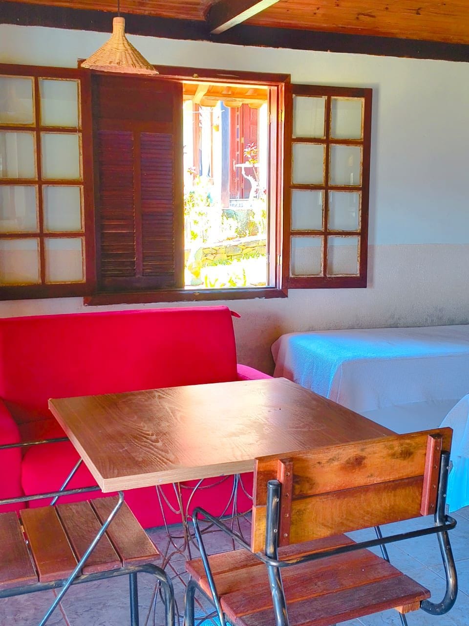 Quarto com mesa de madeira, sofá vermelho e uma cama.