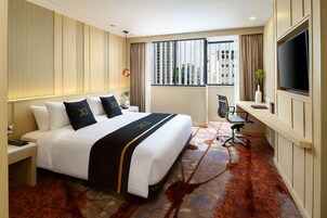 Quarto de hotel com uma cama grande, uma mesa com cadeira, televisão e vista para prédios pela janela.