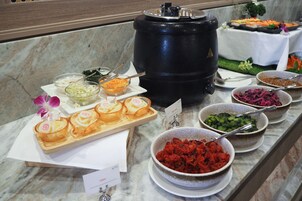 Buffet com diversos itens de comida, incluindo uma grande panela preta, tigelas de legumes e uma bandeja de doces.