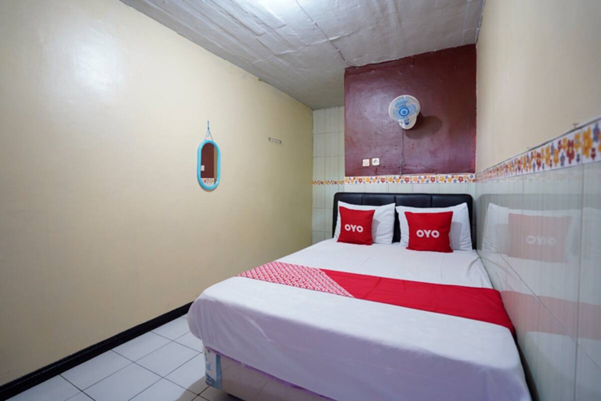 Quarto de hotel com uma cama, dois travesseiros vermelhos, um cobreleite branco e um edredom listrado em vermelho e branco.