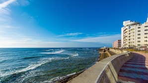 Um calçadão costeiro com vista ampla para o mar e um edifício moderno com varandas.