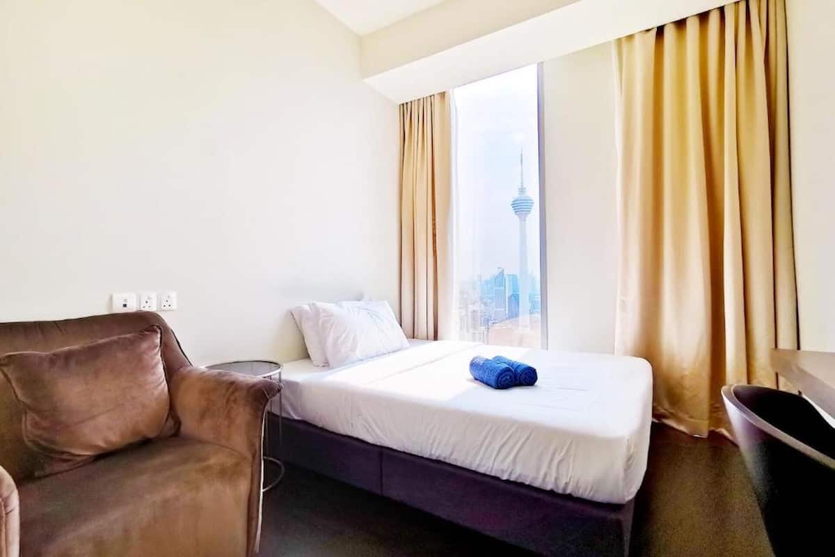 Quarto de hotel com uma cama, uma cadeira, uma janela com cortinas e vista para uma torre.