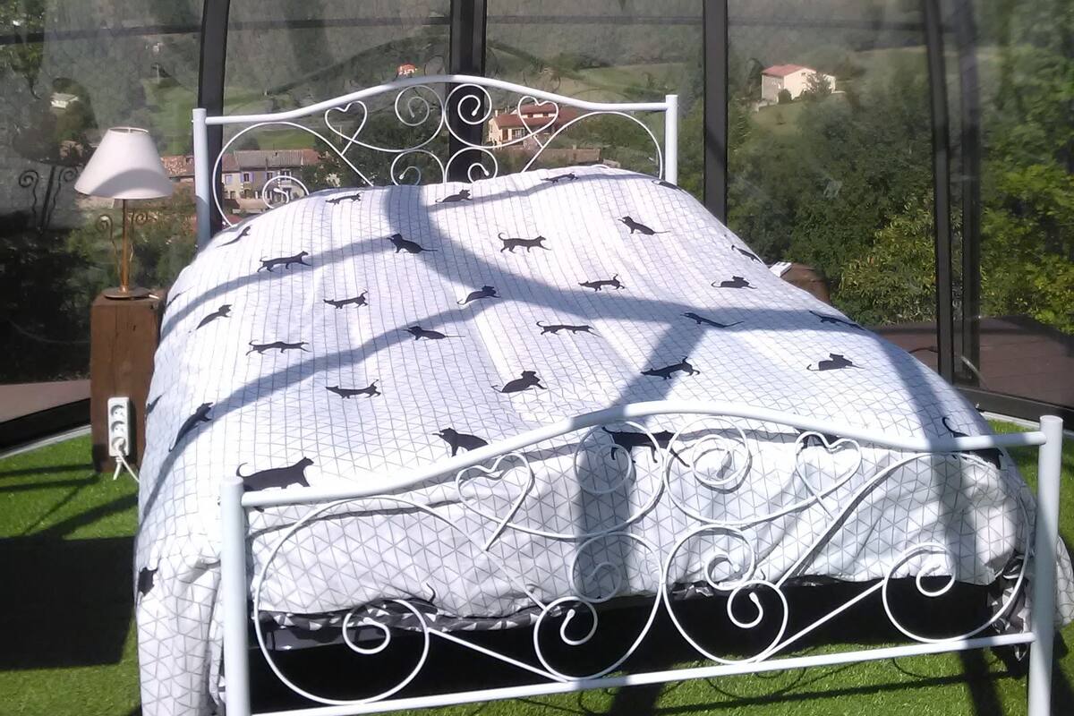 Uma cama com colcha estampada, uma luminária e vista através de uma janela grande.