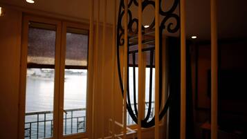 Quarto com vista para um corpo d'água através de grandes janelas, corrimão branco e portão de metal decorativo.