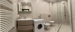 Casa de banho moderna com máquina de lavar embutida, sanita e cabine de duche em vidro.