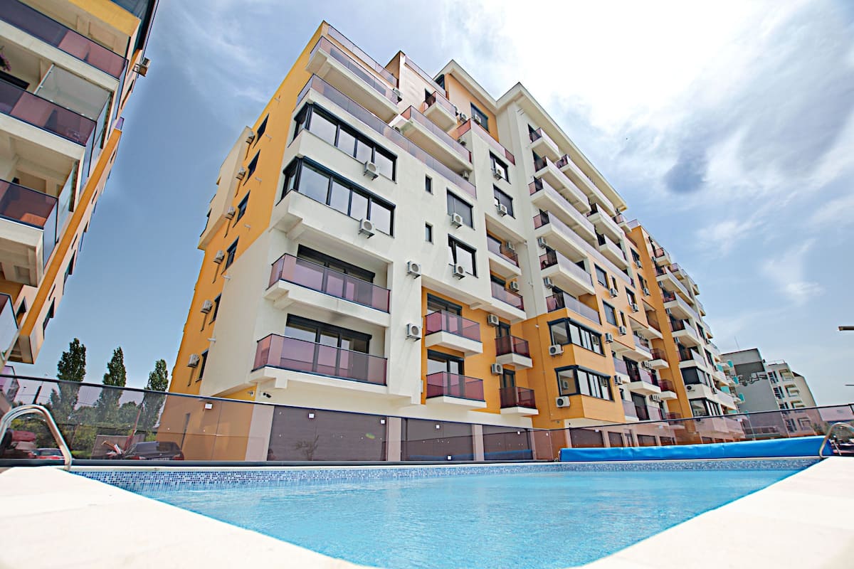 Um edifício residencial de vários andares com varandas, piscina e céu claro.