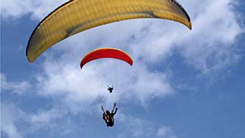 Uma pessoa praticando parapente com um grande paraquedas amarelo e vermelho, ao fundo um céu azul claro.