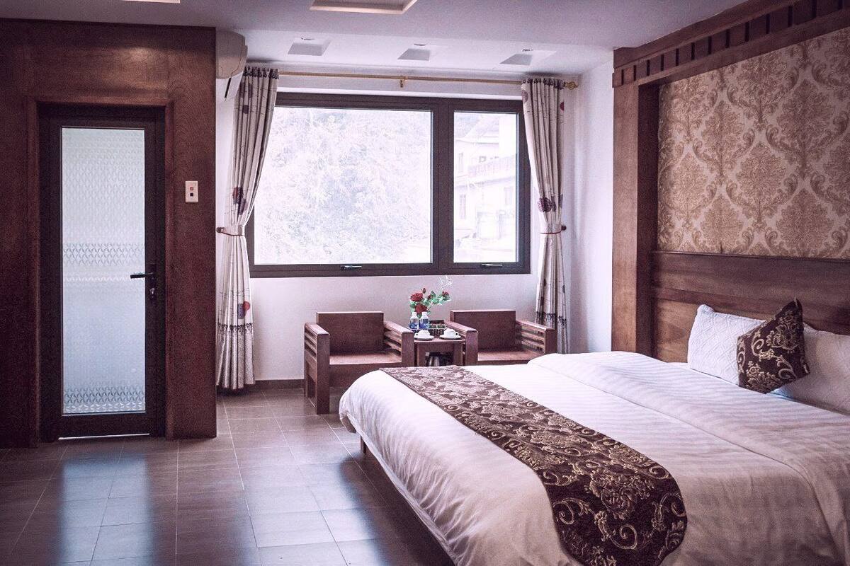 Quarto de hotel com uma cama grande, uma mesa pequena, uma cadeira e uma janela com cortinas.