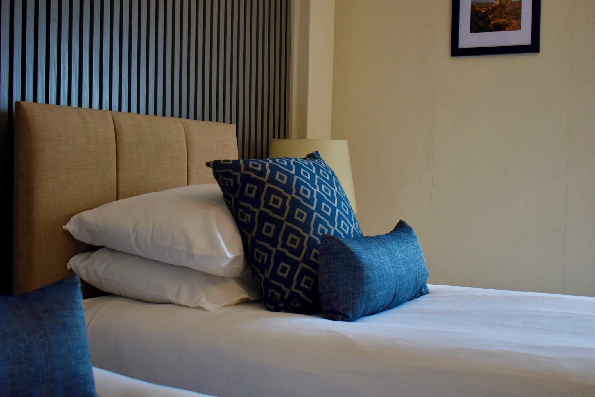 Cama com várias almofadas, cabeceira e parede com linhas verticais.