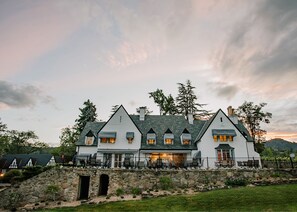 Uma casa grande e branca, de vários andares, com alicerce de pedra, várias chaminés e um gramado bem cuidado.