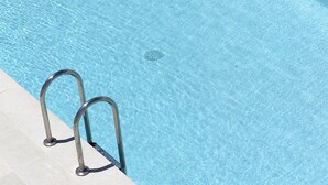 Piscina azul límpida com degraus de metal na borda.