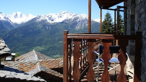 Varanda de madeira com vista para montanhas nevadas e um vale arborizado.