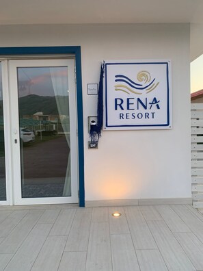 Placa de recepção do RENA RESORT, com vista clara para a porta de entrada e um vislumbre da área circundante.