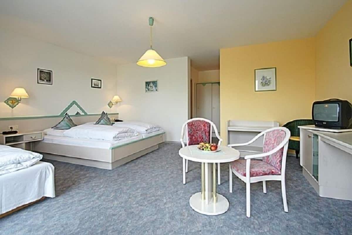 Quarto de hotel com cama, duas mesas de cabeceira, escrivaninha com cadeira, uma mesinha com frutas e uma televisão.
