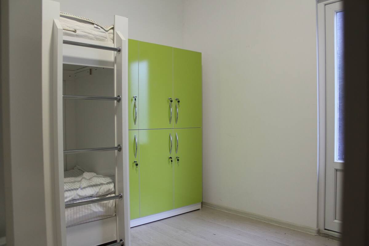 Quarto com guarda-roupa verde, cama branca e uma porta.