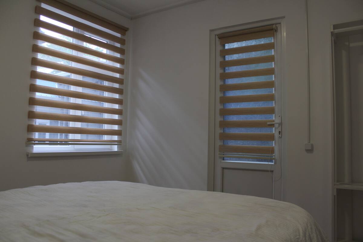Quarto com uma cama, duas janelas com persianas e uma porta.