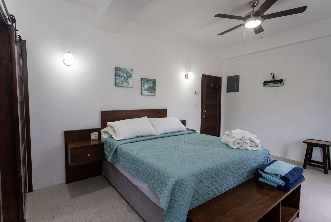 Quarto com cama, mesas de cabeceira, ventilador de teto e obras de arte nas paredes.