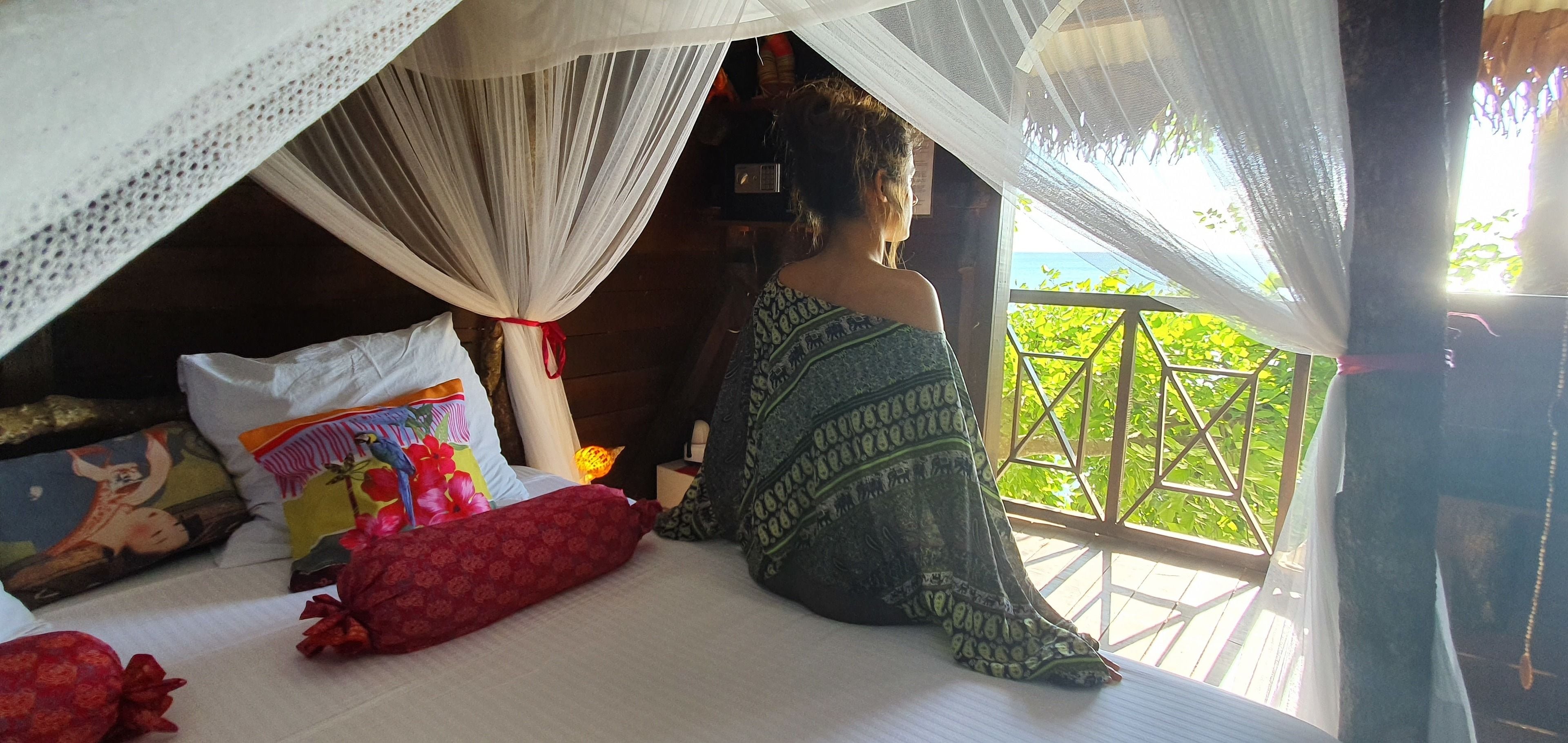 Quarto com cama, janela e vista para área verde, além de mosquiteiro.