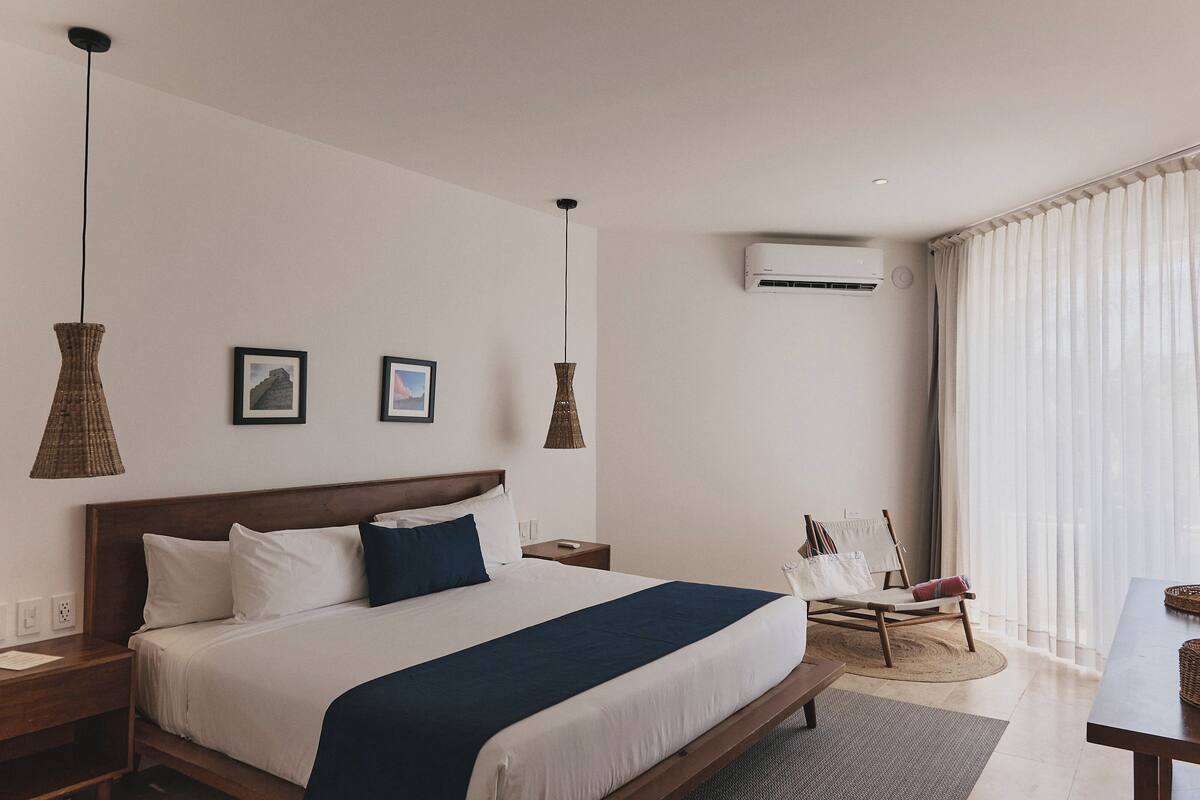 Quarto de hotel moderno com uma cama grande, mesas de cabeceira, escrivaninha e uma cadeira.
