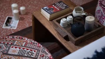 Uma mesinha de madeira com um livro intitulado 'The Silent Sea' de Clive Gussler, uma chaleira, xícaras e um tabuleiro.