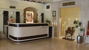 Uma receção com uma placa a indicar "Hotel Grand Safari", uma estátua de um camelo e uma área de receção com chão de mármore.