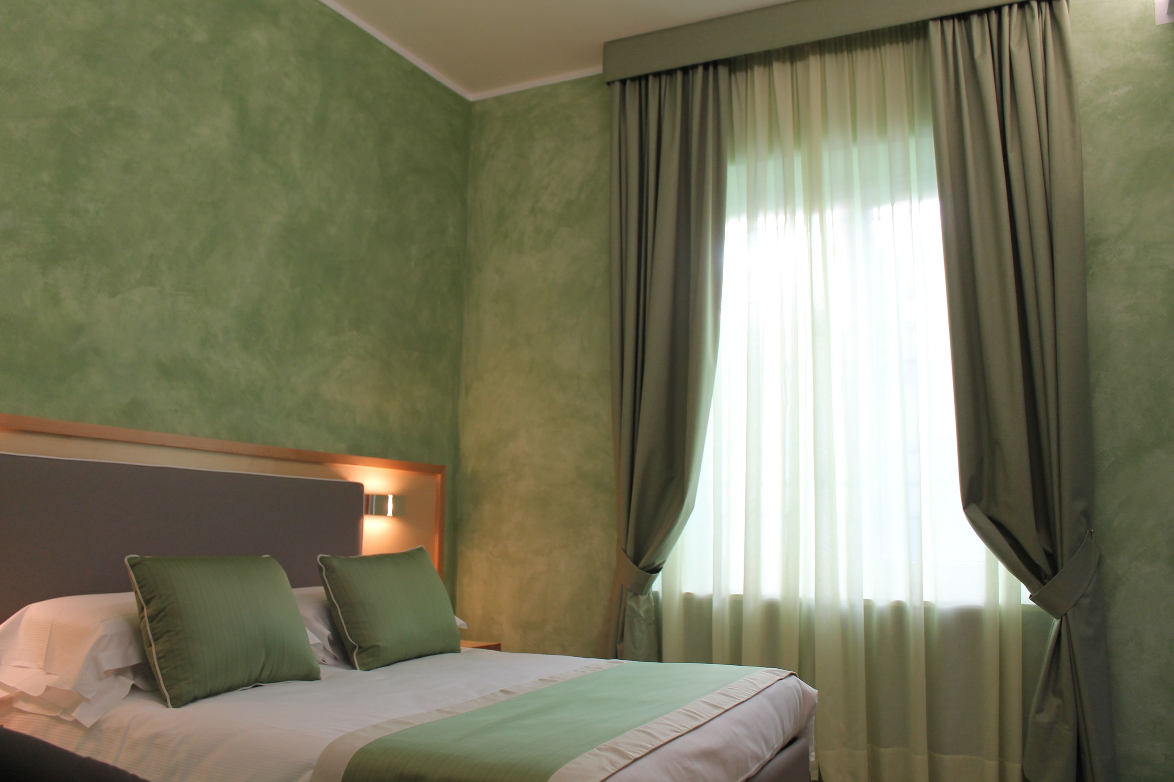 Quarto de hotel com uma cama, cortinas verdes e uma janela com cortinas finas.