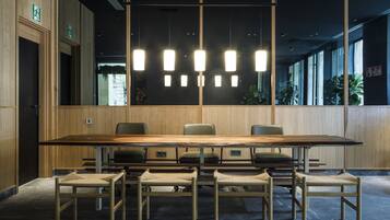 Uma sala de conferências com uma mesa comprida e seis cadeiras, paredes de madeira e luminárias pendentes.