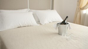 Uma cama com roupa de cama branca, um balde com uma garrafa e copos, e uma cabeceira.