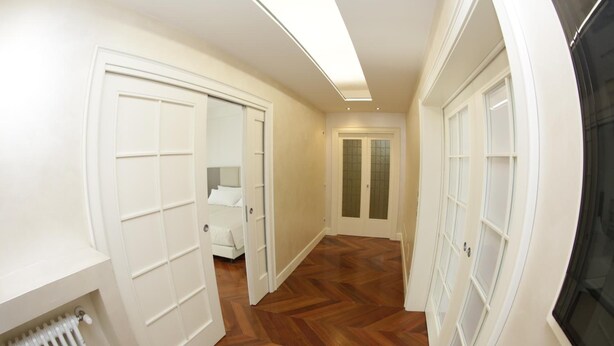 Um corredor com piso de madeira, portas brancas e um radiador.