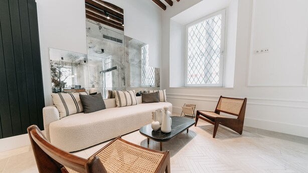 Uma sala de estar moderna com um sofá, duas cadeiras de madeira, uma mesa de centro e um espelho grande.