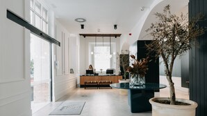 Um lobby de hotel moderno com piso em padrão herringbone, um balcão de recepção e uma grande árvore em vaso.