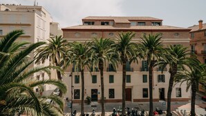 Um edifício com telhado em cerâmica, várias janelas e palmeiras na frente.