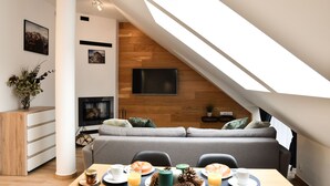 Uma sala de estar moderna com área de jantar, apresentando uma parede de madeira, TV de tela plana e um ambiente acolhedor.
